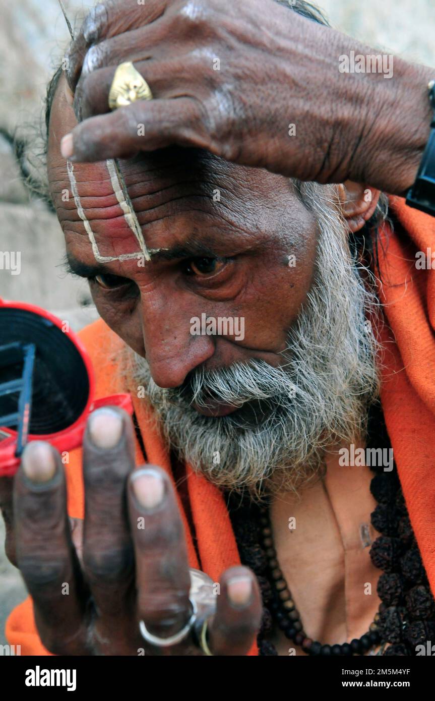 A sadhu painting his forehead with Tilaka on the Mallick Ghat by the ...