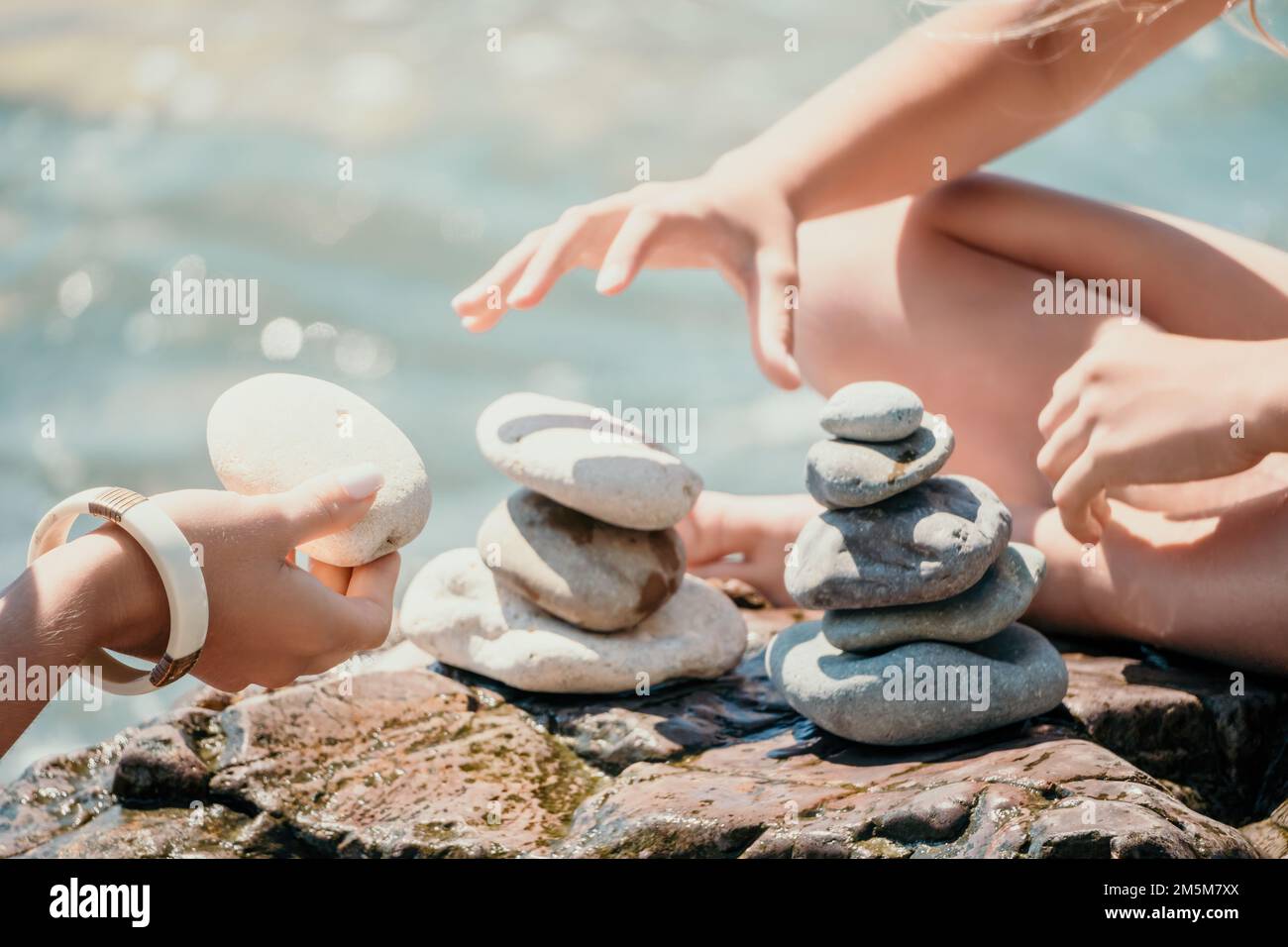 Woman with daughter bilds stones pyramid on seashore on a sunny day on ...