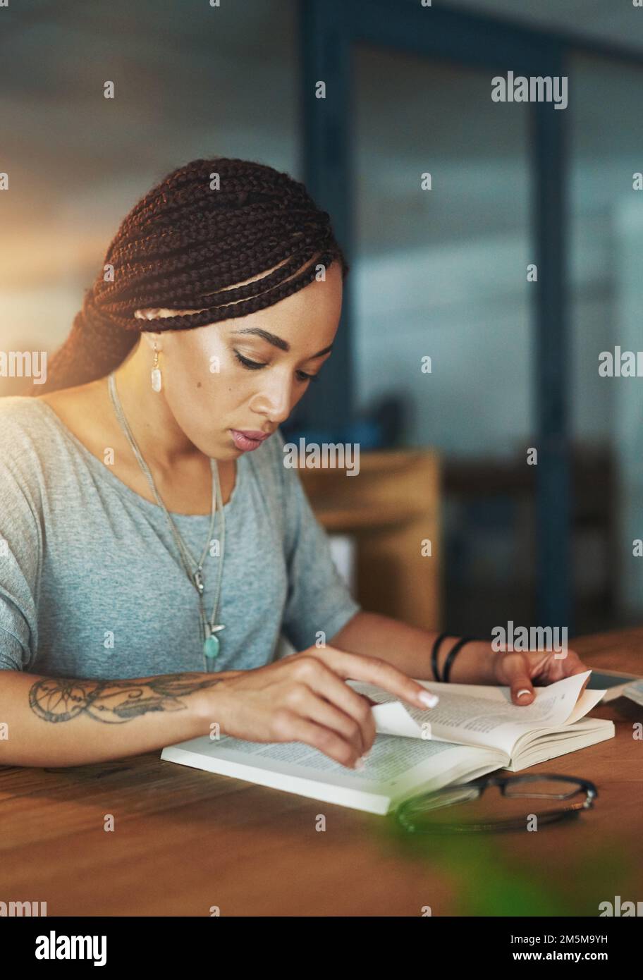 Getting into a good book. a young woman reading a book while working ...