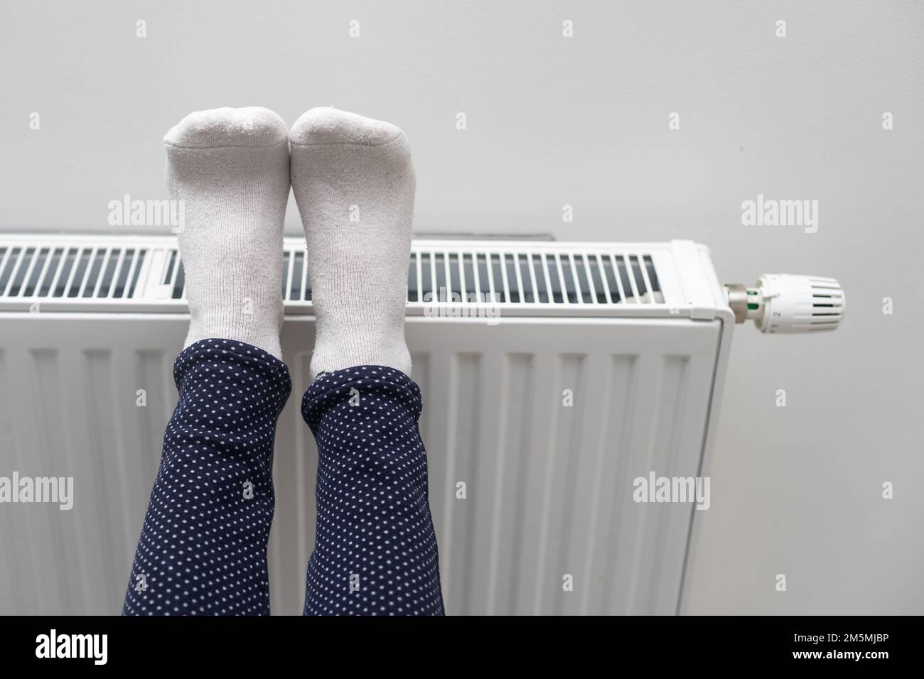 Woman warming up with feet on heater Winter socks drying on a heater ...