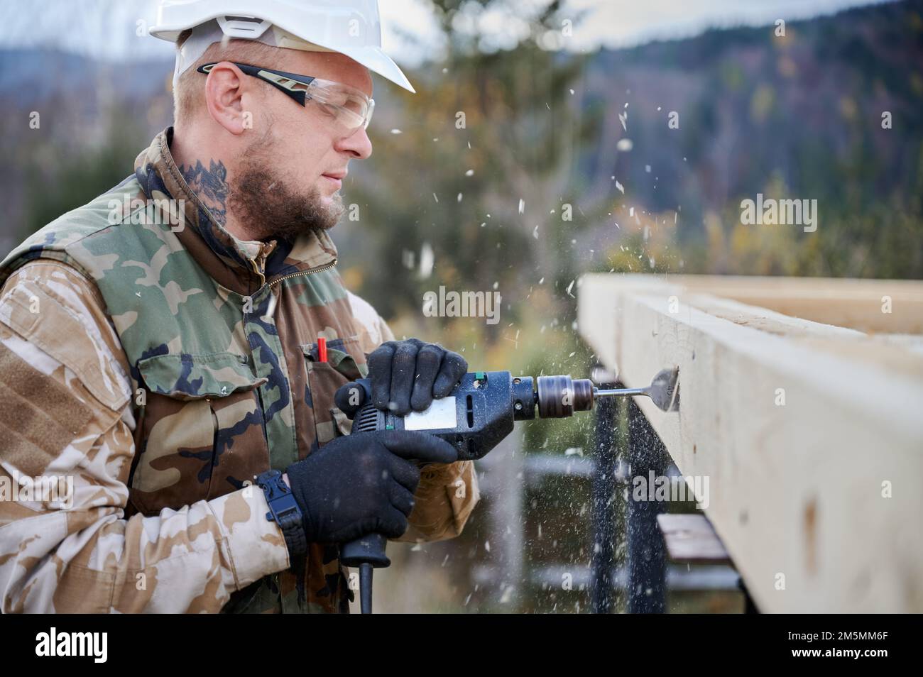 Man building wooden frame house. Worker drilling hole by electric drill ...