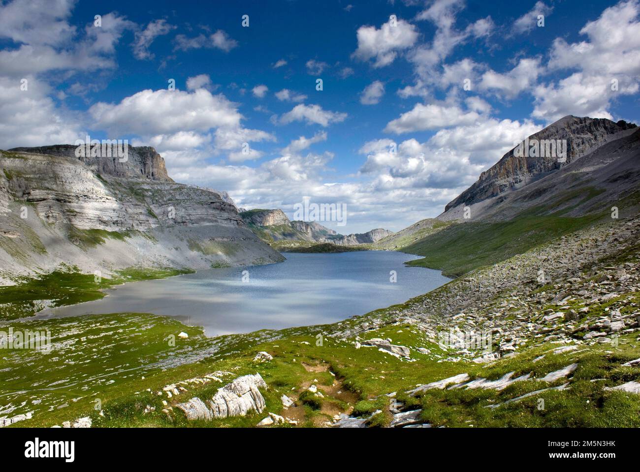 A small lake surrounded by big mountains with the blue sky reflected in ...