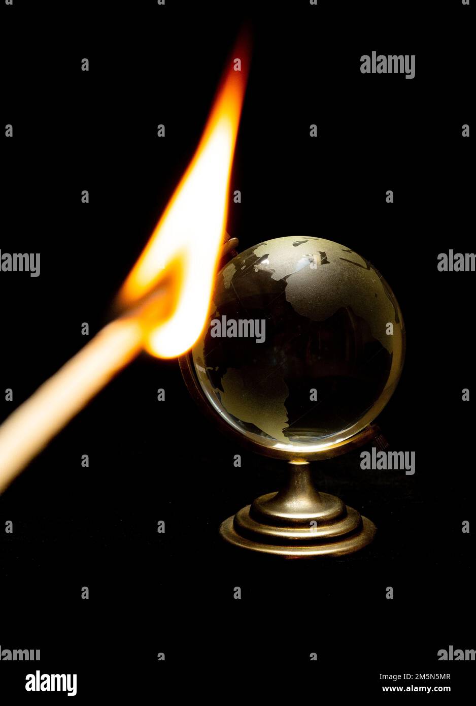 A vertical shot of a match with fire and a globe on the black ...