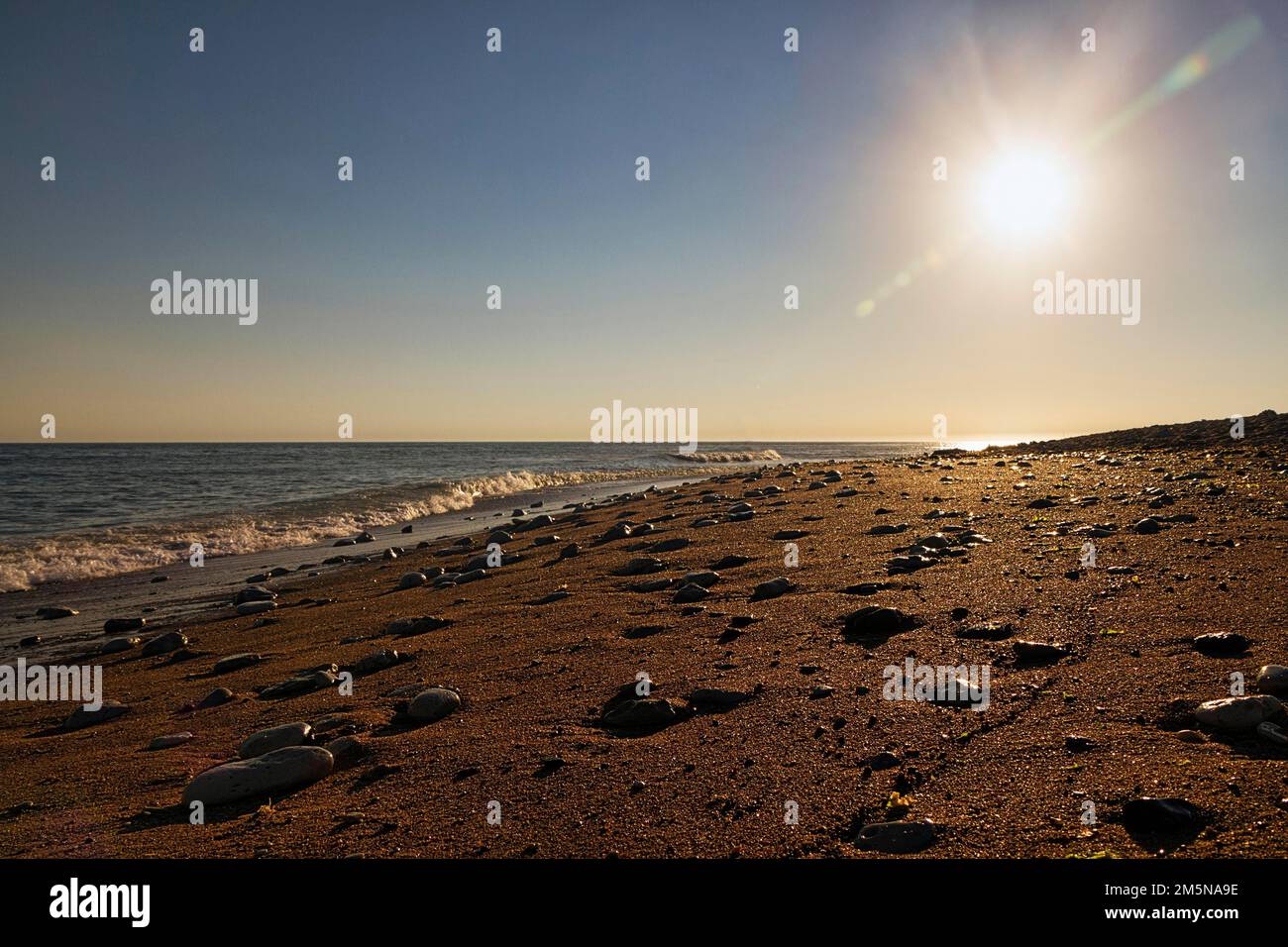 Pebbles glistening on the empty sandy beach, sunbeams and light ...