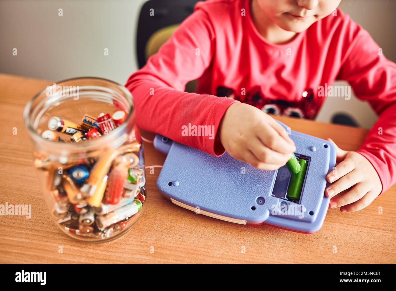 Little girl removing used batteries from toy and putting into jar for ...