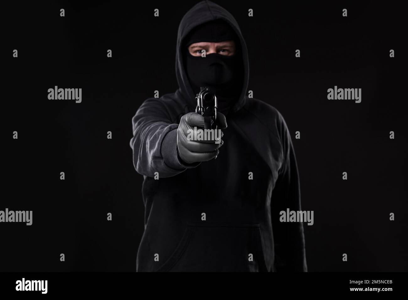 Masked robber with gun aiming into the camera against a black ...