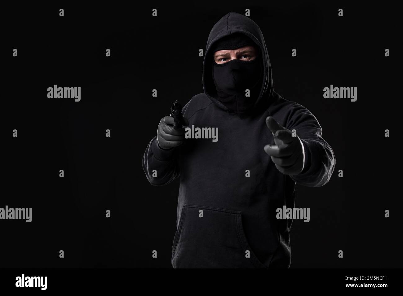 Masked robber with gun aiming into the camera against a black ...