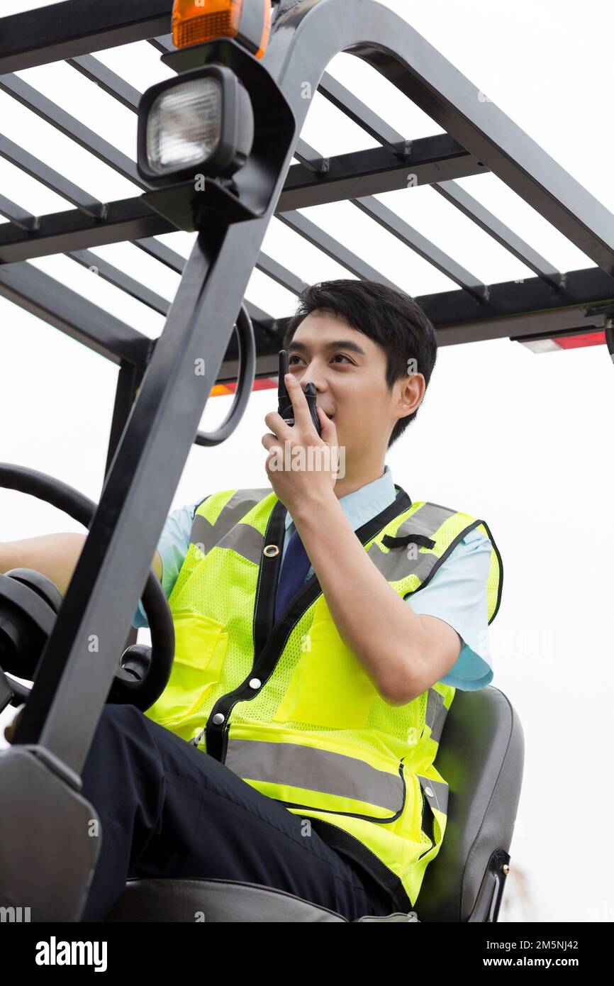 Logistics warehouse workers driving forklift truck, hand interphone ...