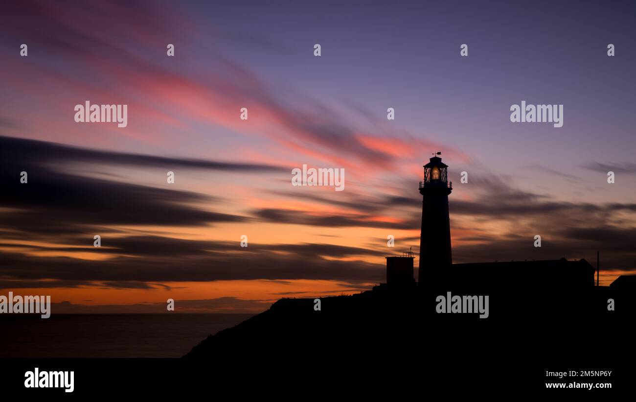Lighthouse at sunrise with coloured sky and sea creating silhouette ...