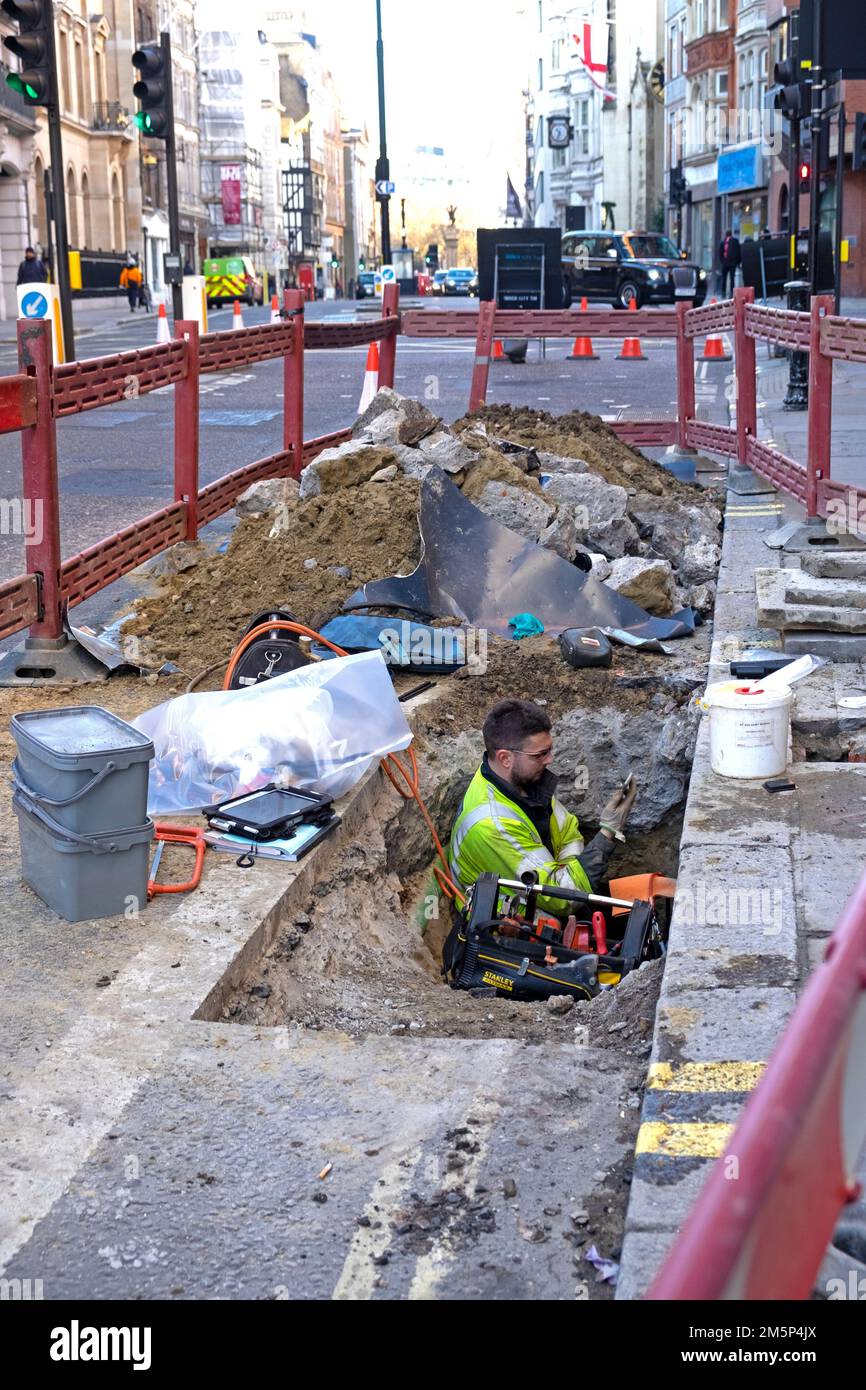 Workman looking at mobile phone while working in roadworks hole dug up ...