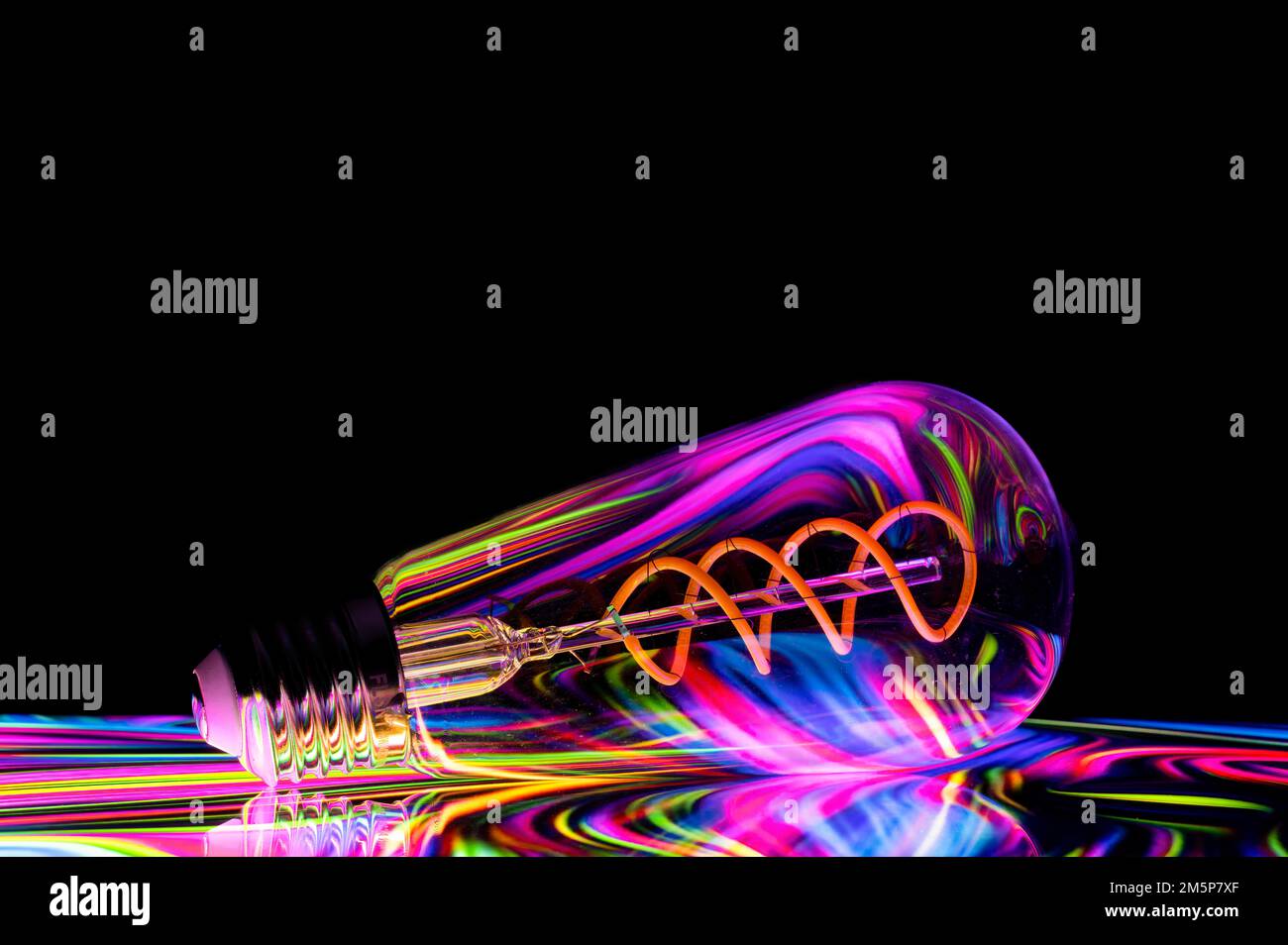 Colourful patterns reflect within a clear glass, oval shaped lightbulb ...