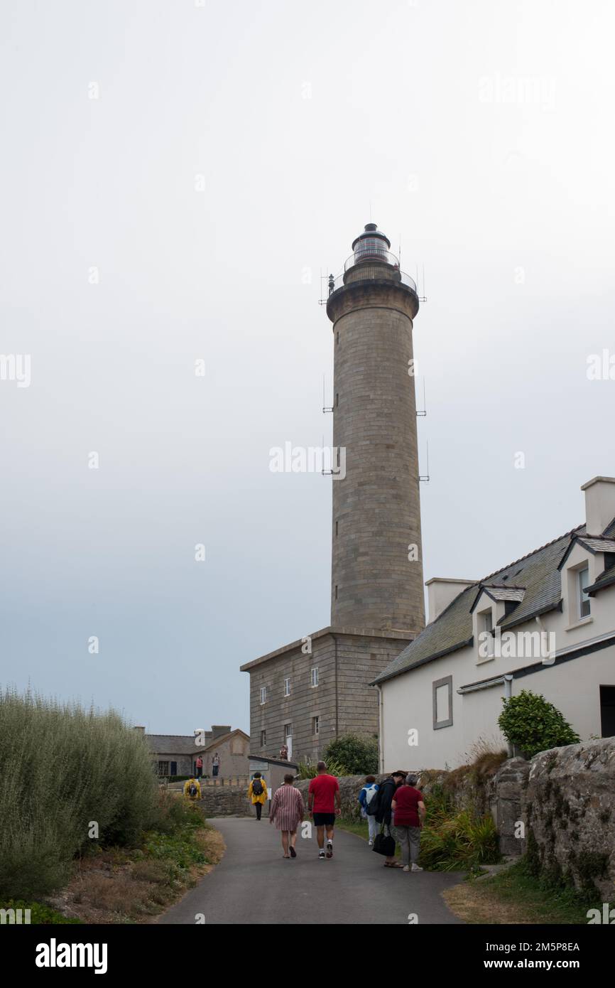 A vertical of people walking towards a lighthouse on the Isle of Batz ...