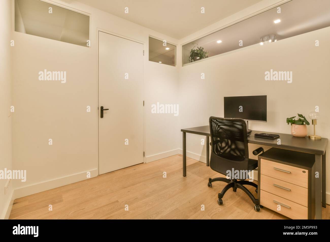 a home office with white walls and wood flooring, including a black ...