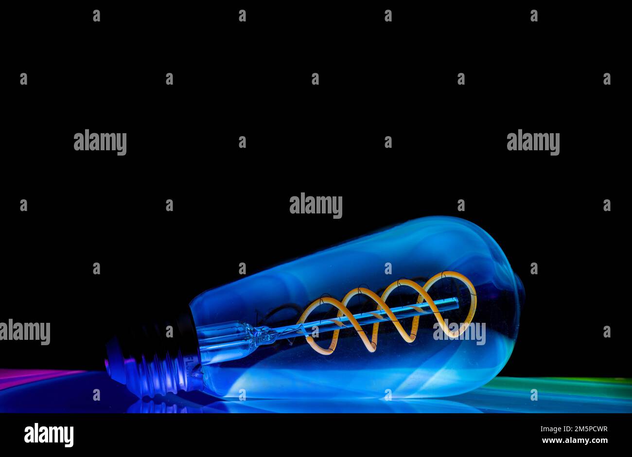 Colourful patterns reflect within a clear glass, oval shaped lightbulb ...