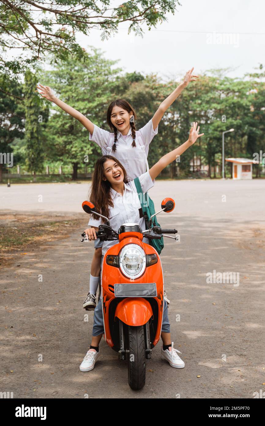 Two high school girls riding motorbikes standing while celebrating ...