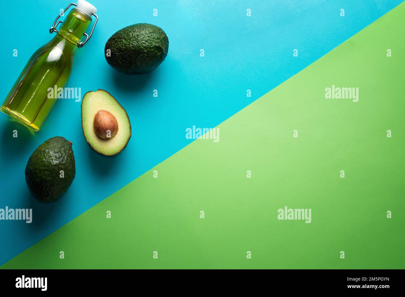 Fresh avocados on a blue and green background. Avocado oil in a bottle ...