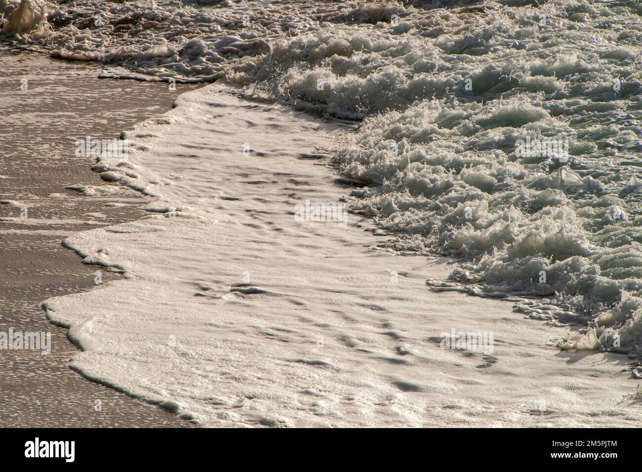 Gentle ocean waves wash onto the sandy shoreline of Praia da Cresmina near Guincho, Portugal ...