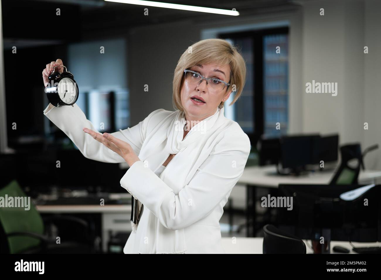 Caucasian business woman showing on alarm clock in office Stock Photo ...