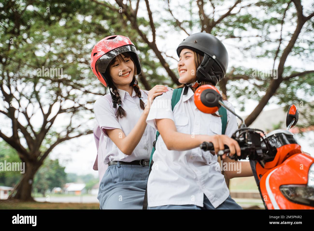 Two student girls wearing helmets chatting while riding a motorcycle ...