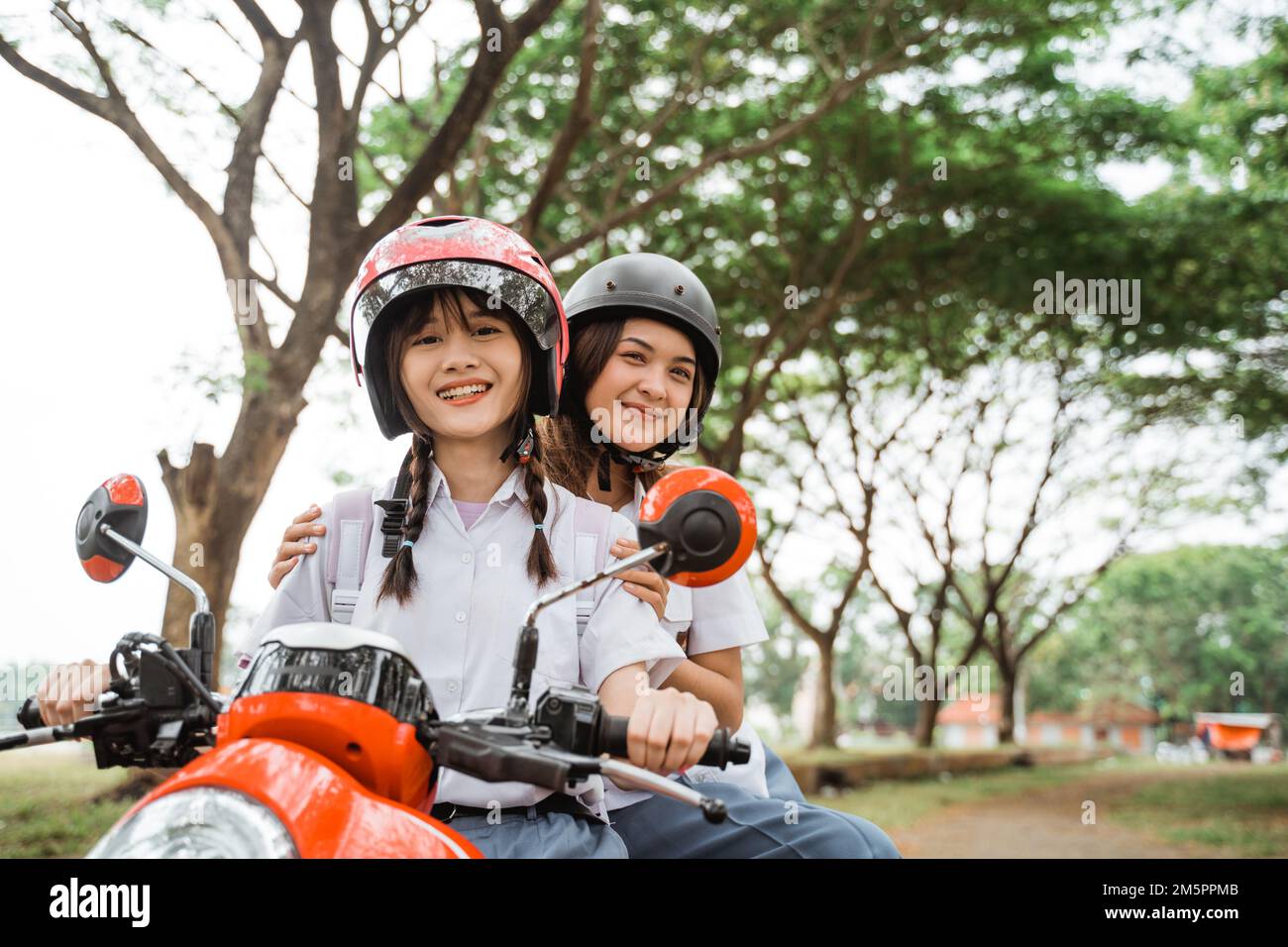 Two beautiful high school students smiling while riding a motorcycle ...