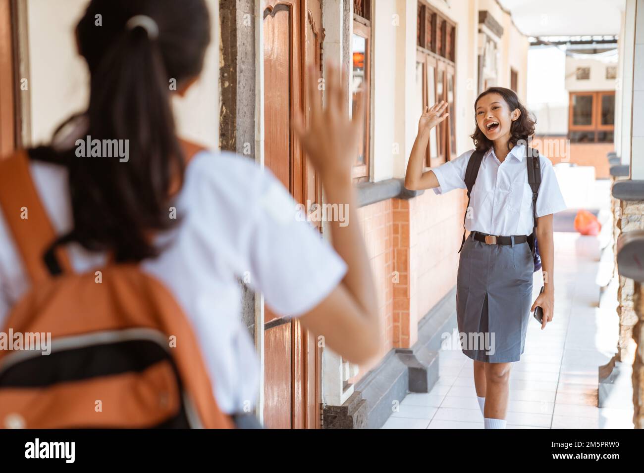 high school girl greets by waving when meeting her friend Stock Photo ...