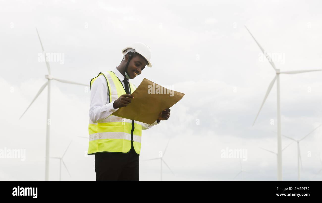 African engineer man stands holding blueprint front the wind turbines ...