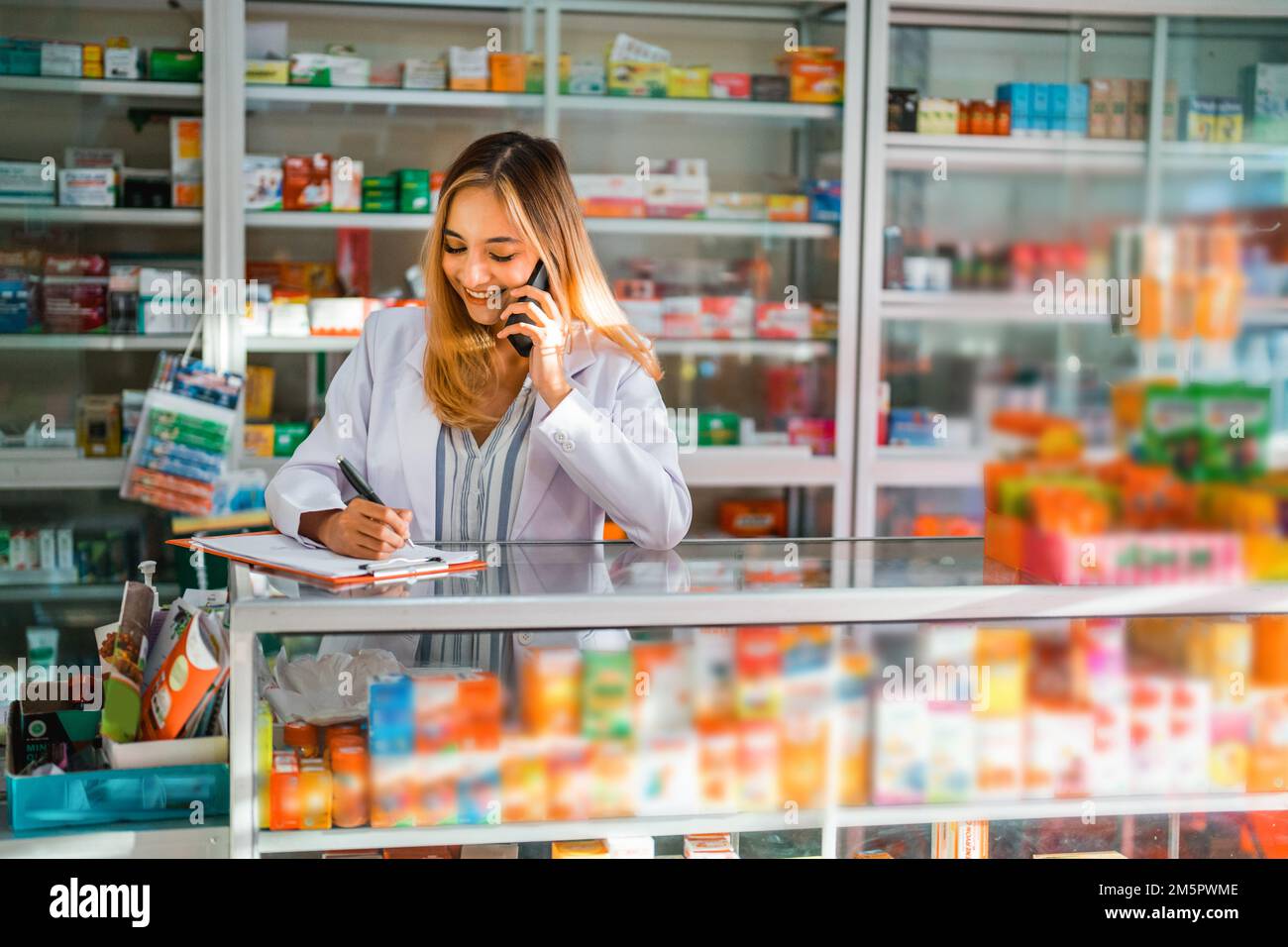 Attractive female pharmacist making a call while writing on paper Stock ...