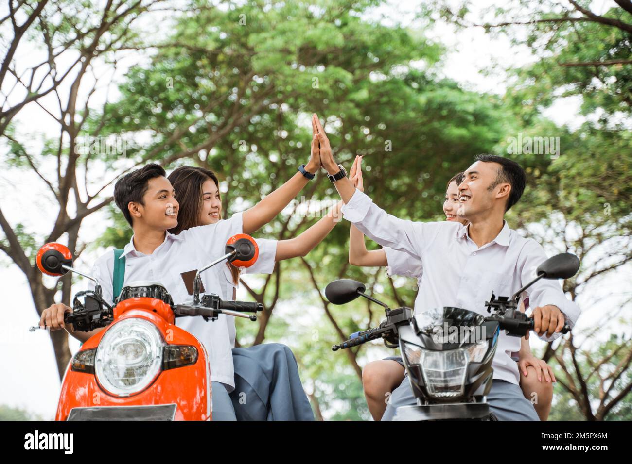 Four students clapping with their friends while riding a motorbike ...