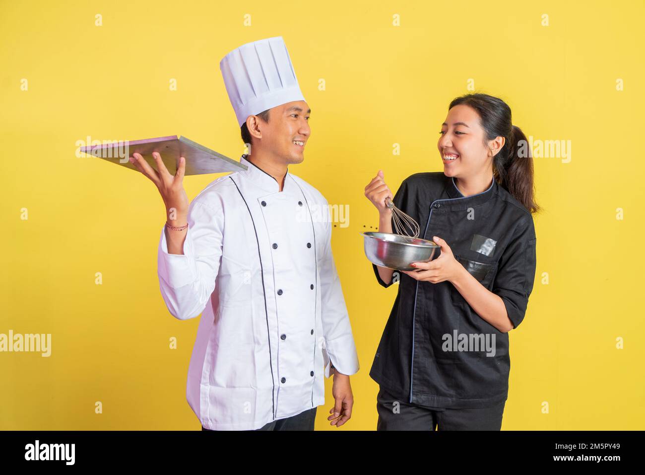 male chef carrying bread tray and female chef using whisk Stock Photo ...