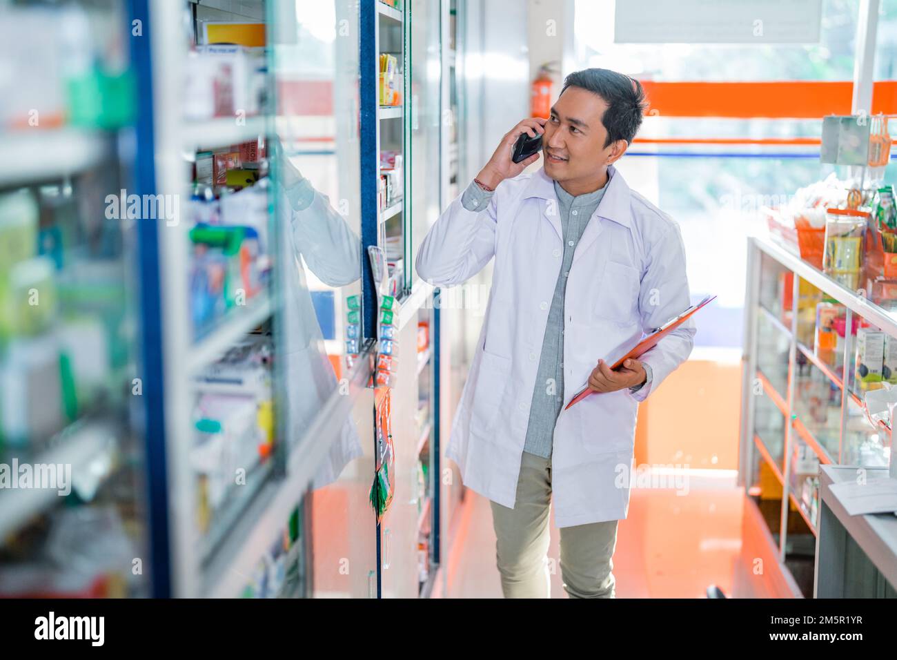 male pharmacist in uniform making phone call while holding clipboard ...