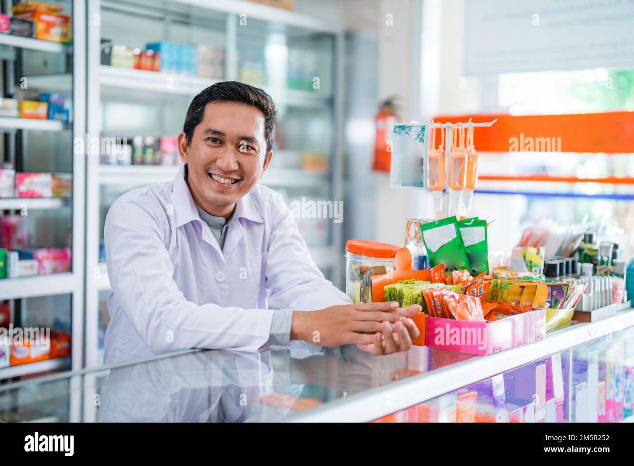 male pharmacist in uniform standing behind display case in pharmacy ...