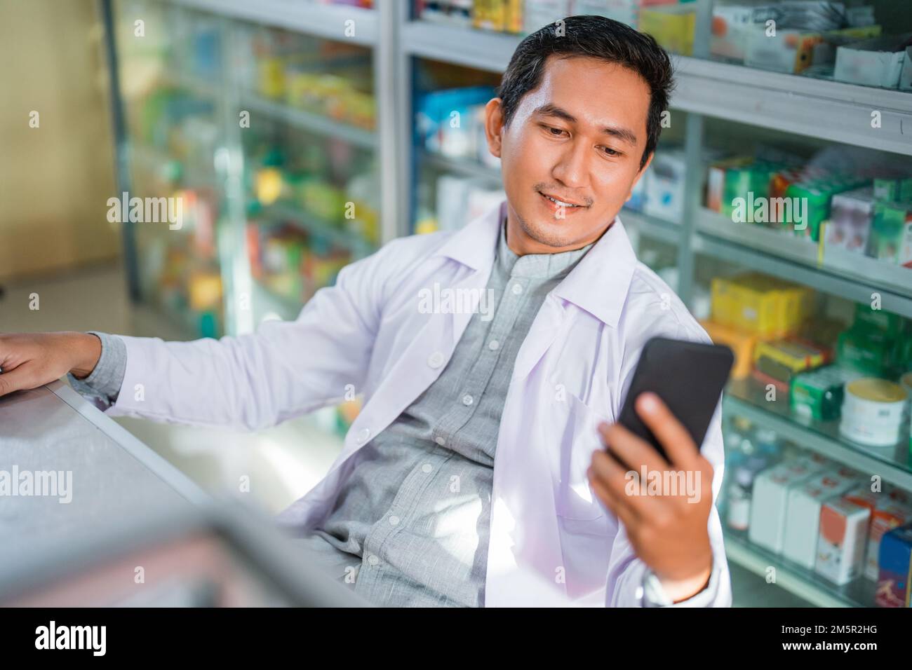 Asian male pharmacist in uniform working while using smartphone Stock ...