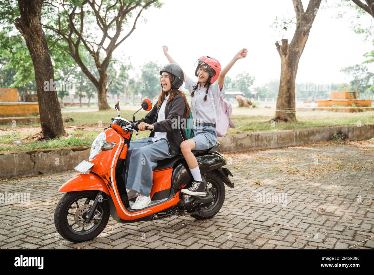 Two high school student girls happily riding motorbikes Stock Photo - Alamy