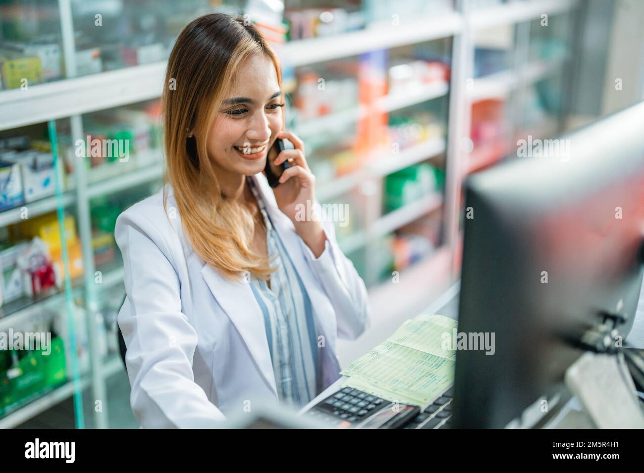 Beautiful pharmacist working in front of computer monitor while calling ...