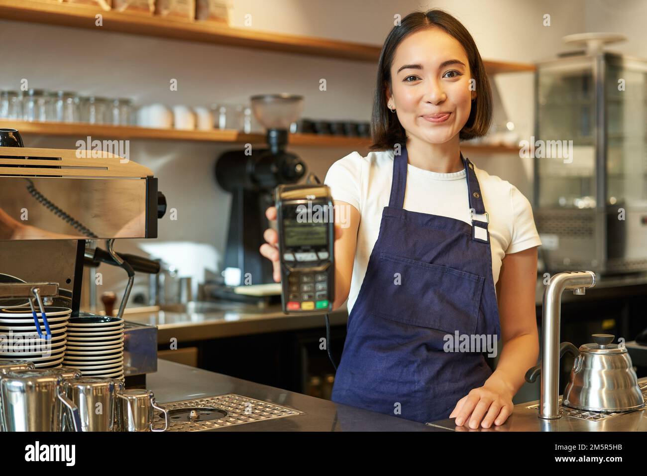 Smiling asian barista, coffee shop staff gives you credit card machine ...