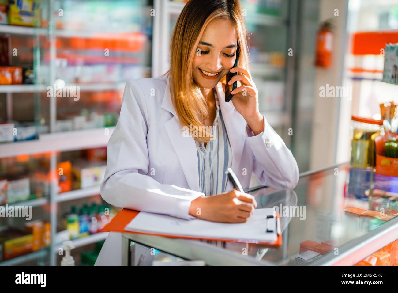 beautiful pharmacist making a call while writing request on paper Stock ...