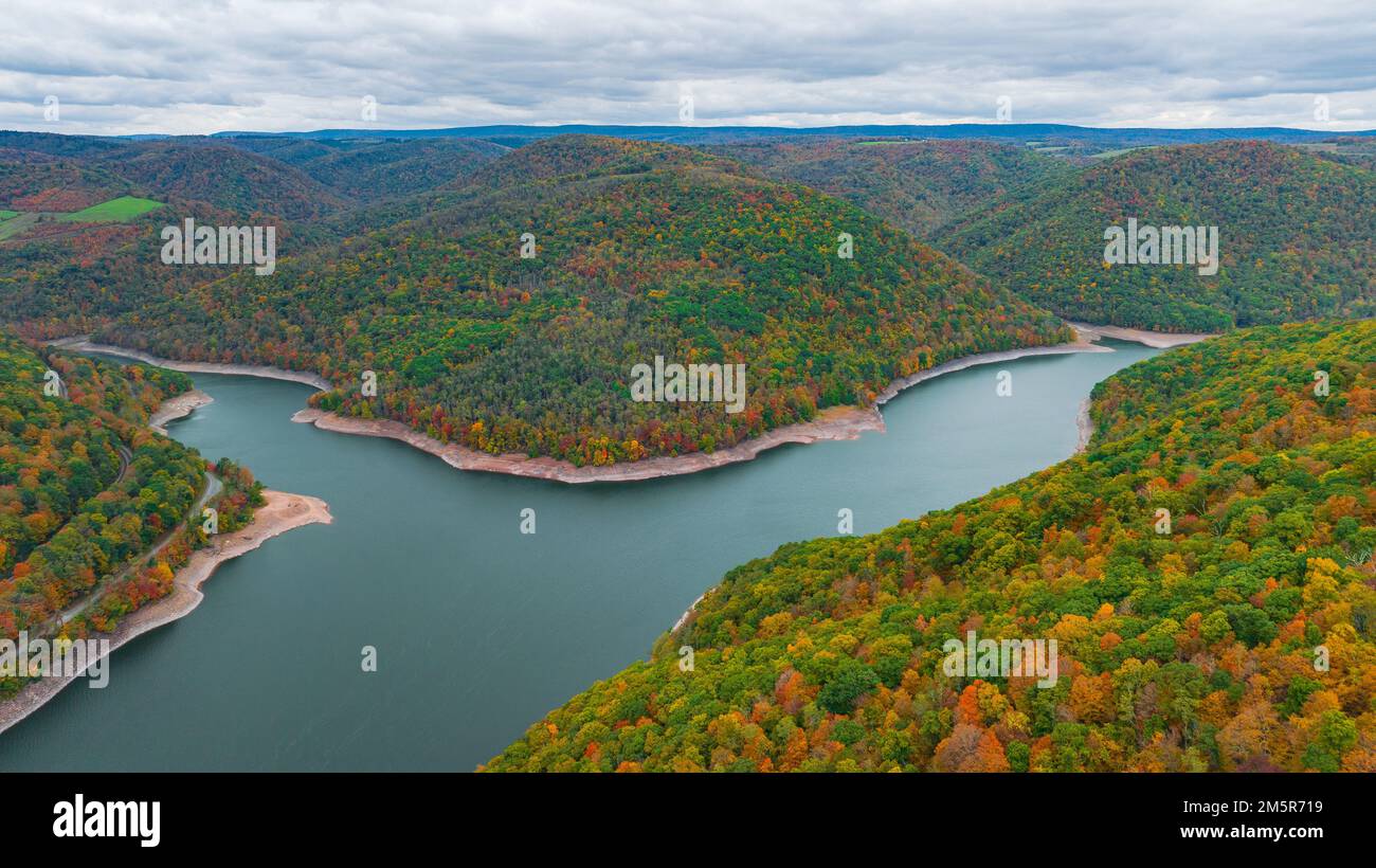 An aerial of a scenic lake surrounded by a dense forest with autumn ...