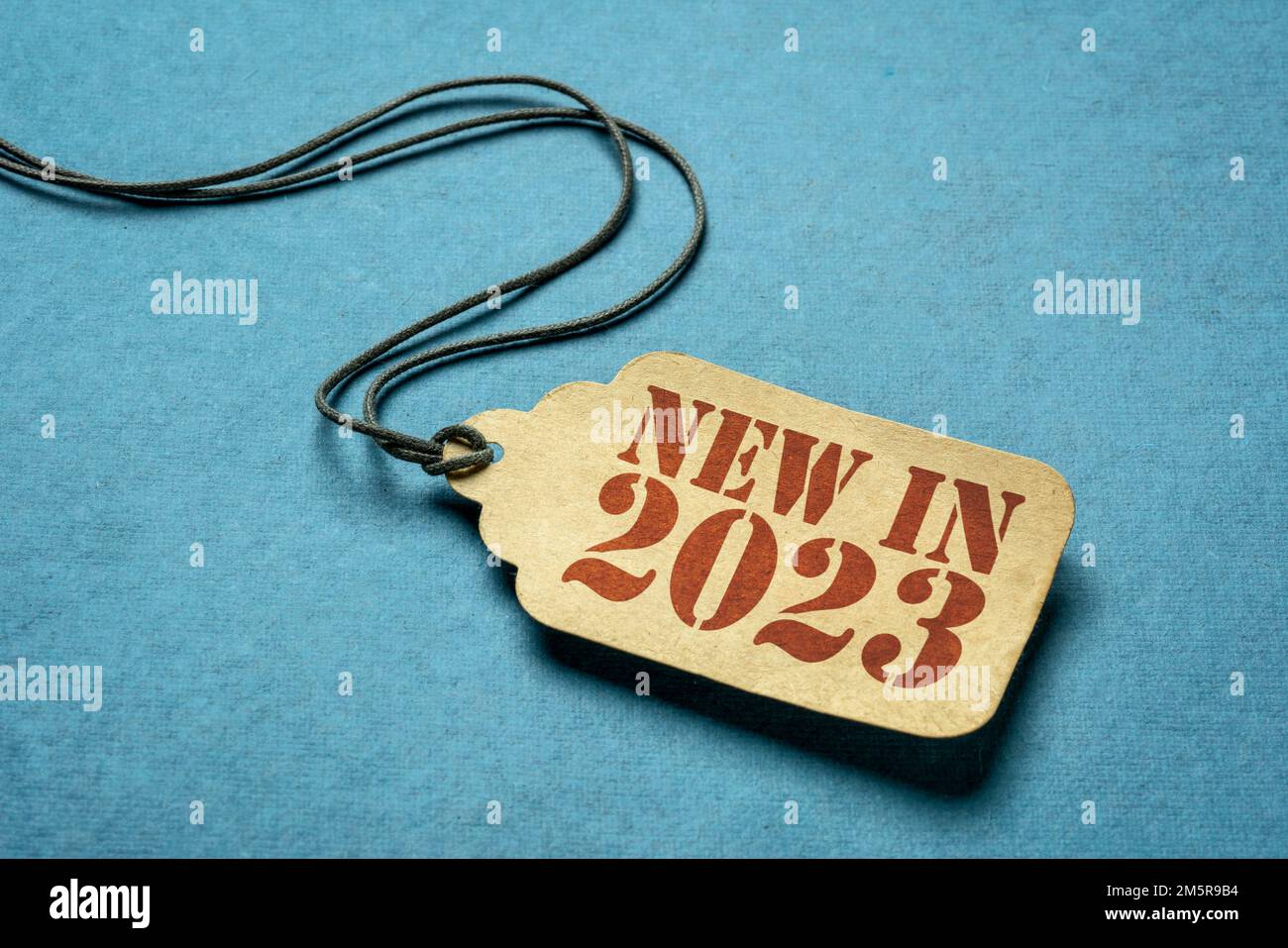 new in 2023 - red stencil text on a paper price tag against blue paper ...