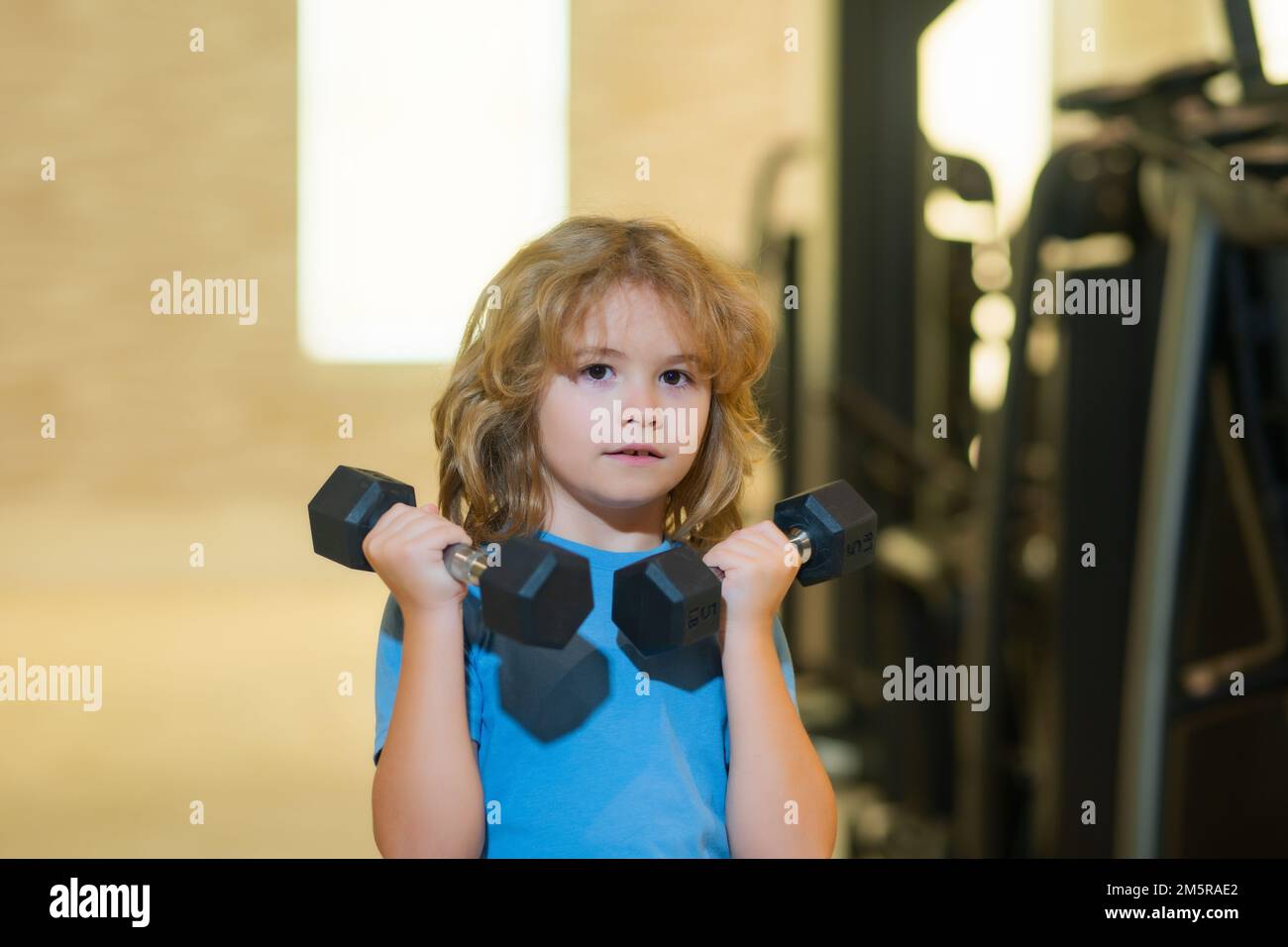 Cute little boy doing exercises with dumbbells. Portrait of sporty child with dumbbells. Happy ...