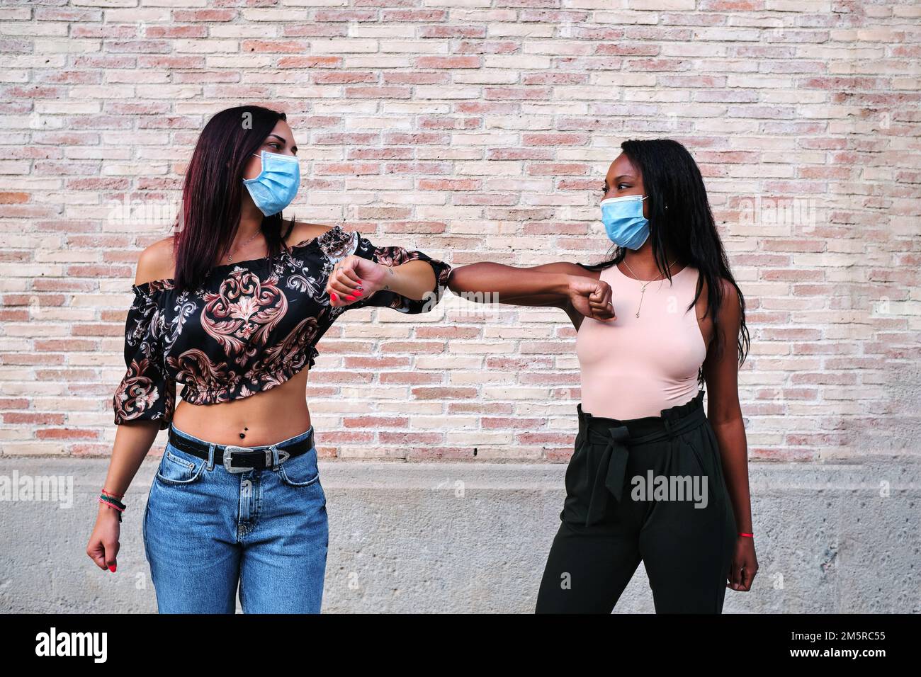 Multiethnic friends with mask waving with the elbows Stock Photo - Alamy