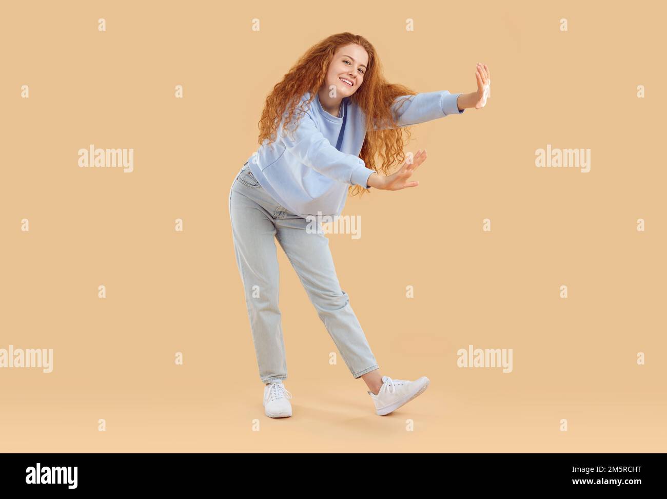 Happy smiling young ginger woman in casual clothes dancing on beige ...