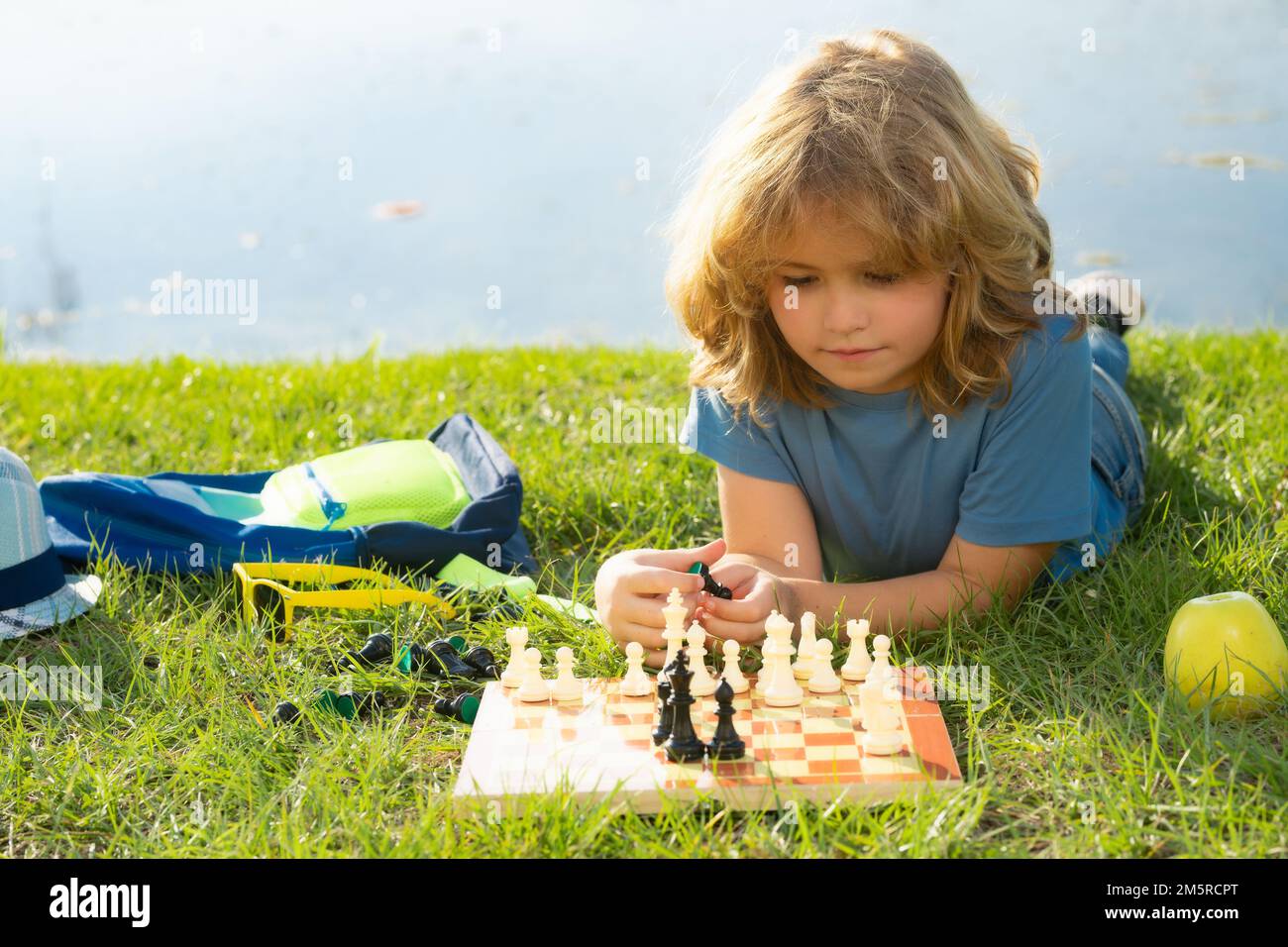 Kid playing chess game in backyard, laying on grass. Concentrated child ...