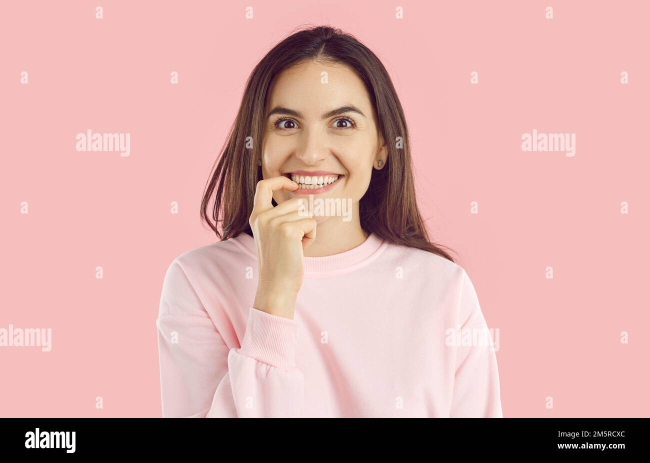 Excited young woman biting finger as cunning looking at camera Stock ...