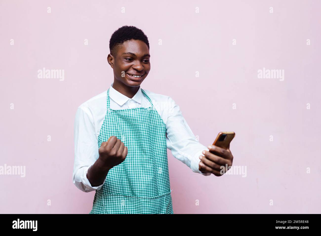 A cheerful young African cook holding and looking at a smartphone in ...