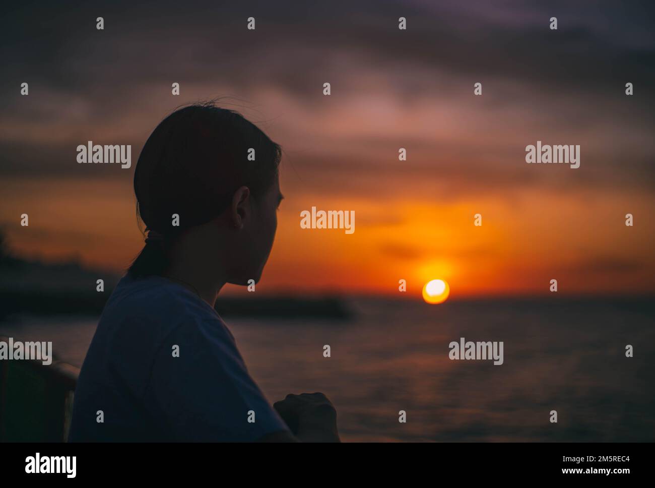 A selective focus of a woman watching the sun and the sea during golden ...