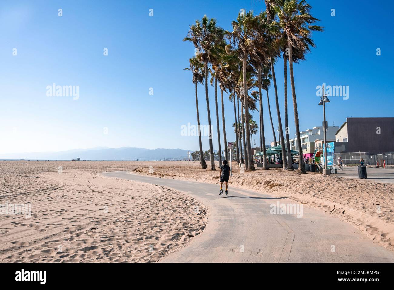 Rear view of man roller skating on road amidst sand at Venice beach ...