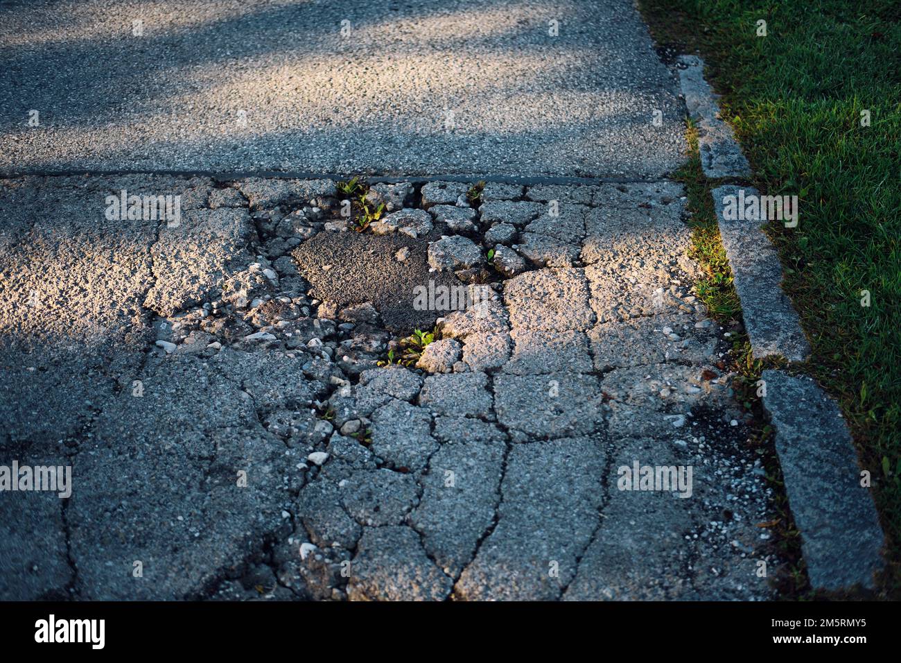 The cracked and damaged street near the green grass with sunlight ...