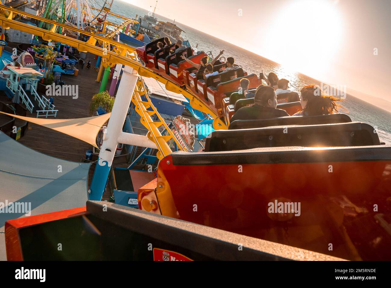 People enjoying roller coaster with view of bright sun over sea at ...