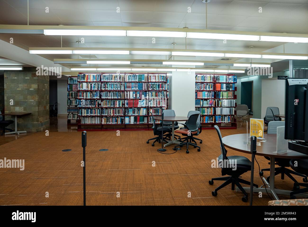Books on shelves with empty chairs and tables in illuminated library at ...