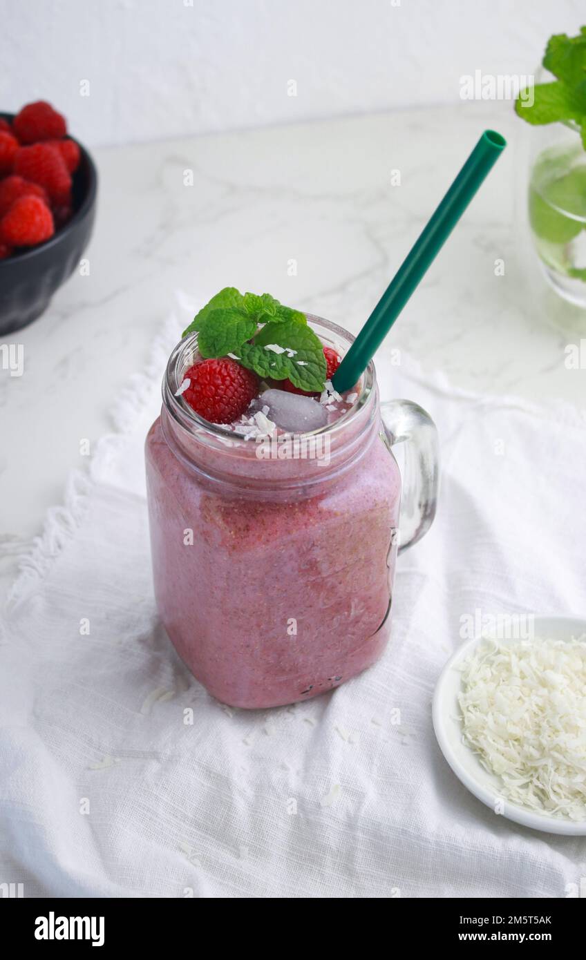 raspberry coconut smoothie with ice in a jar with straw, white ...